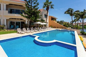 Piscina com espreguiçadeiras e um edifício com varandas ao fundo.