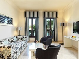 Uma sala de estar moderna com sofá, duas poltronas, uma mesa de centro, televisão e uma janela grande com cortinas.