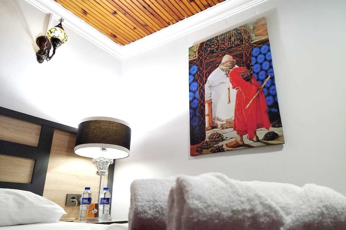 Quarto de hotel com teto de madeira, uma pintura de um casal, uma luminária e uma cama com uma toalha.