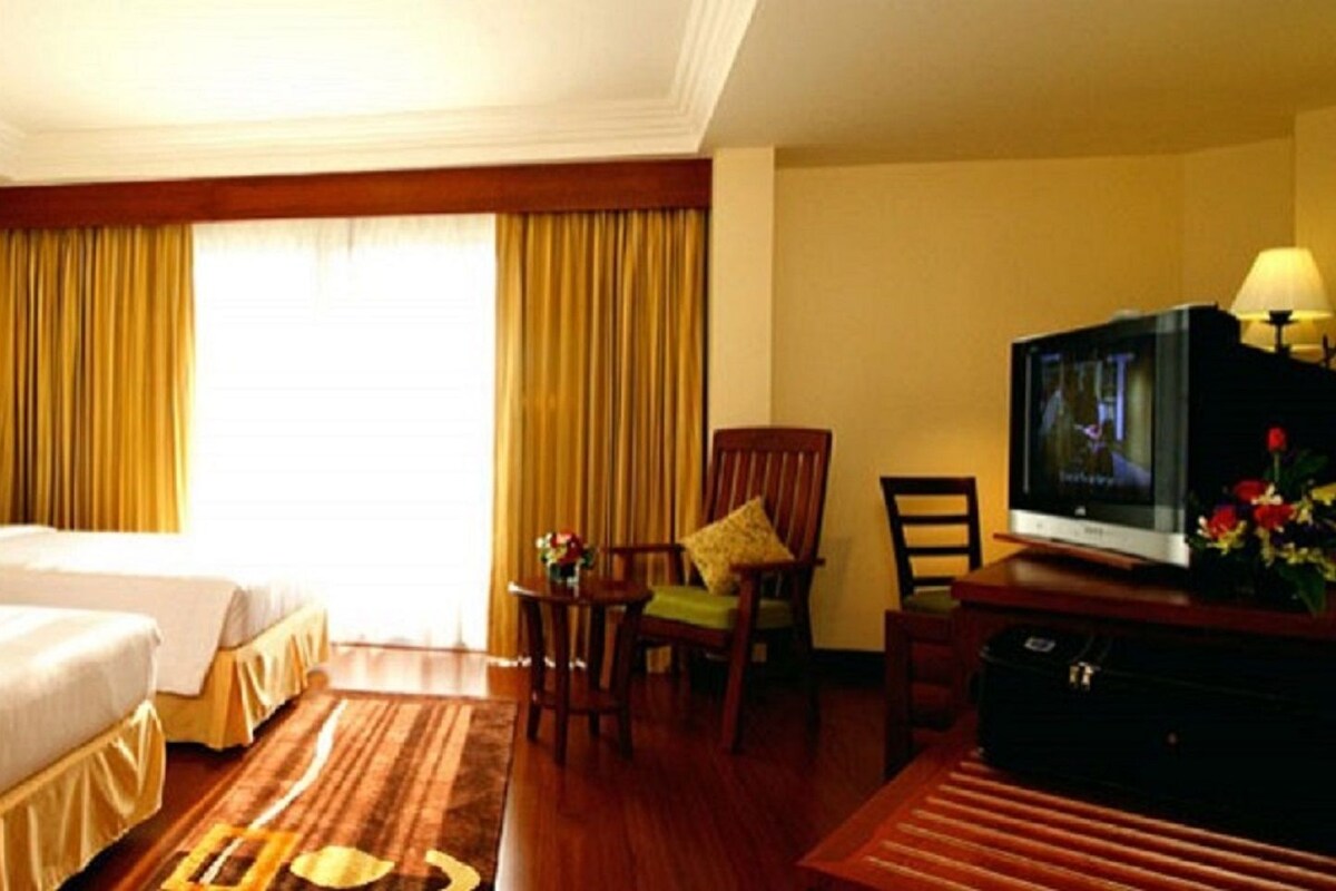 Quarto de hotel com duas camas, televisão, escrivaninha e uma cadeira.