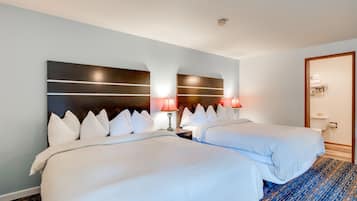 Quarto de hotel com duas camas, uma cabeceira grande fixada na parede, abajures e um tapete azul.