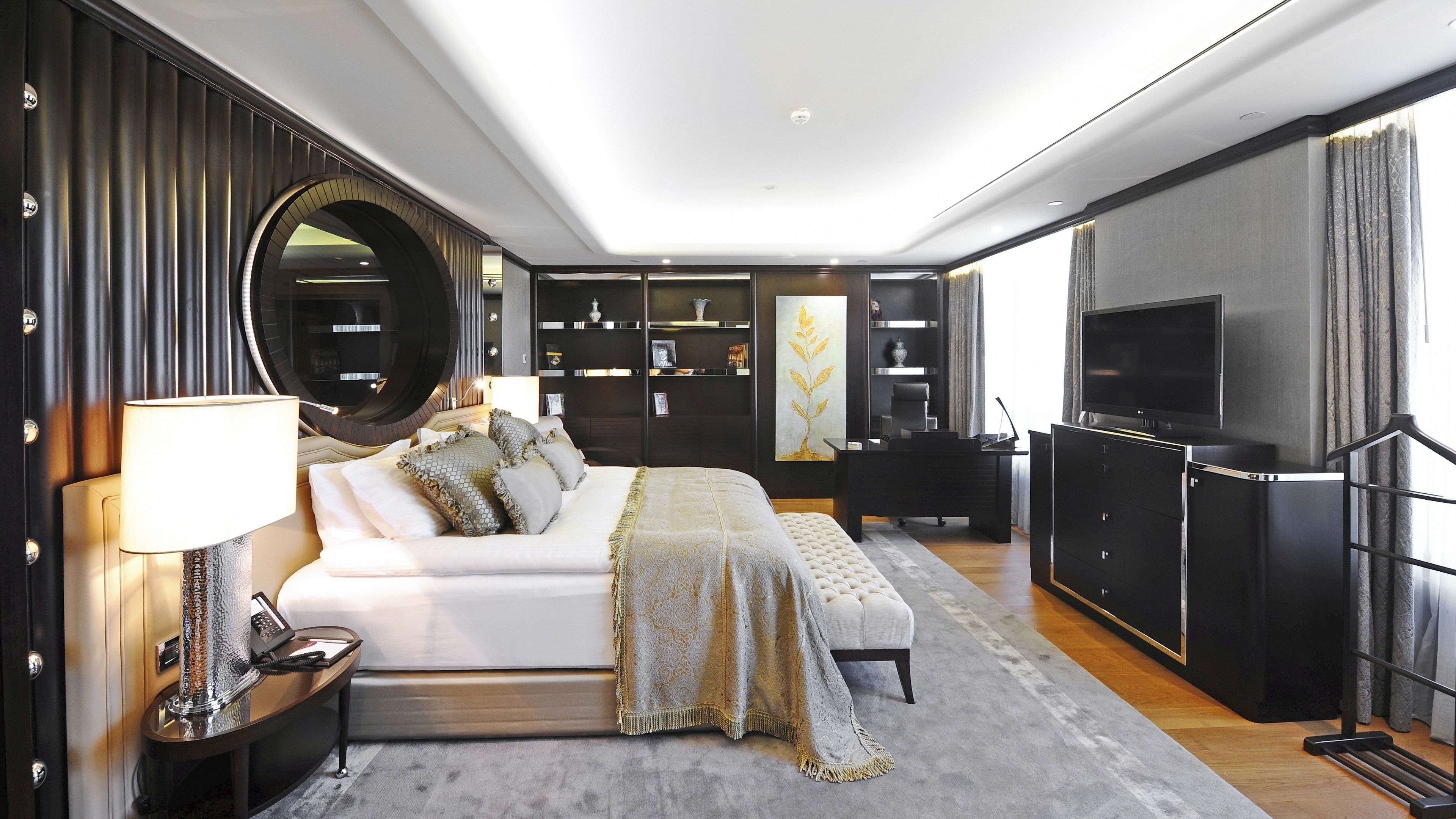 Quarto moderno com uma cama grande, mesas de cabeceira, televisão, guarda-roupa e espelho.