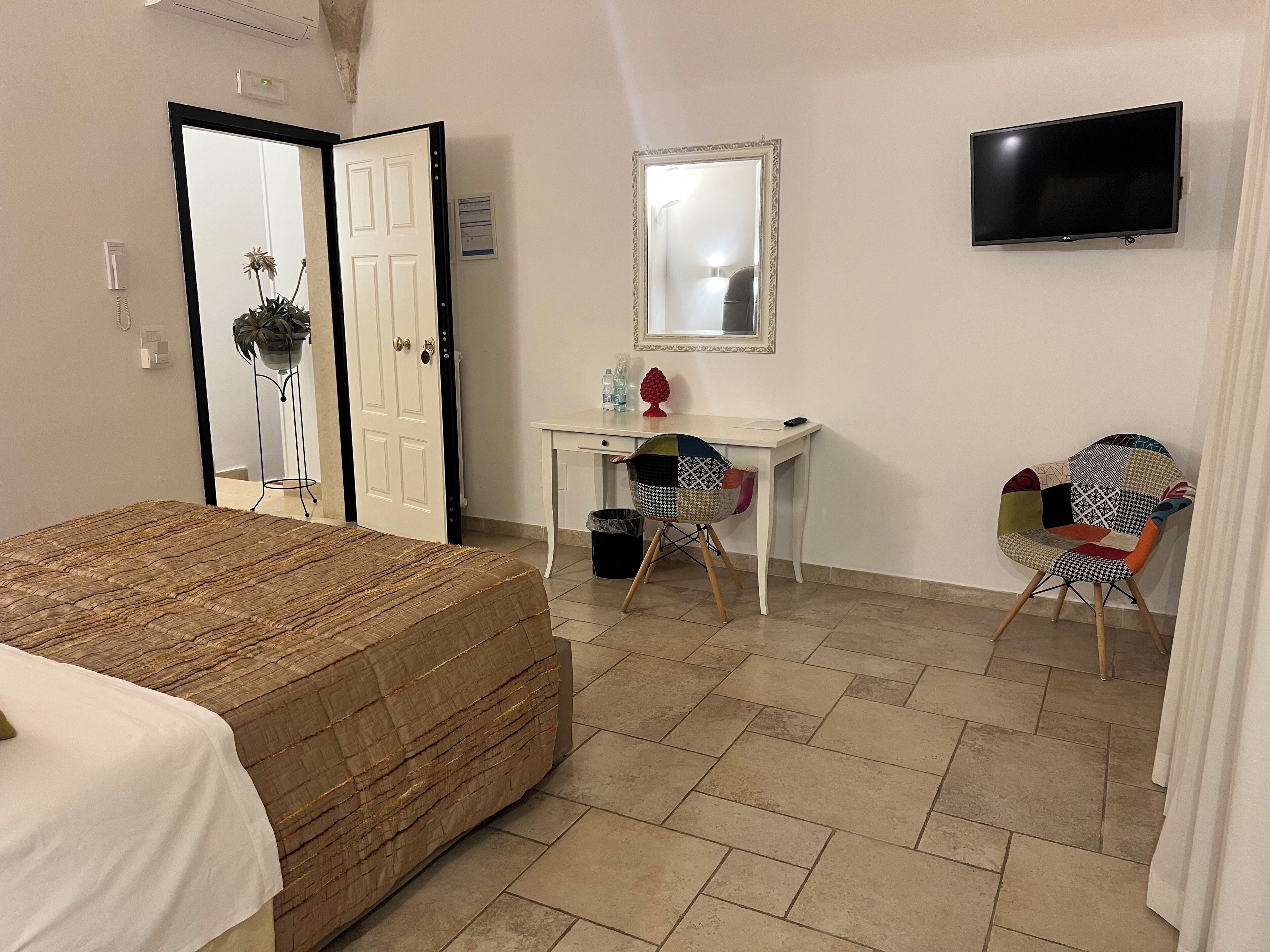 Quarto com uma cama, escrivaninha com cadeira, televisão e porta.
