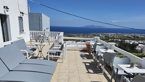 Terraço no telhado com espreguiçadeiras e mesas, com vista para o mar e montanhas ao longe.