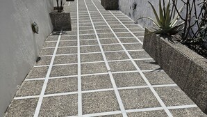 Uma trilha de azulejos conduz a uma entrada de prédio com uma parede branca e um arco de pedra.
