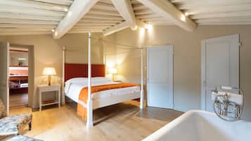 Quarto com cama de dossel, banheira branca e piso de madeira.
