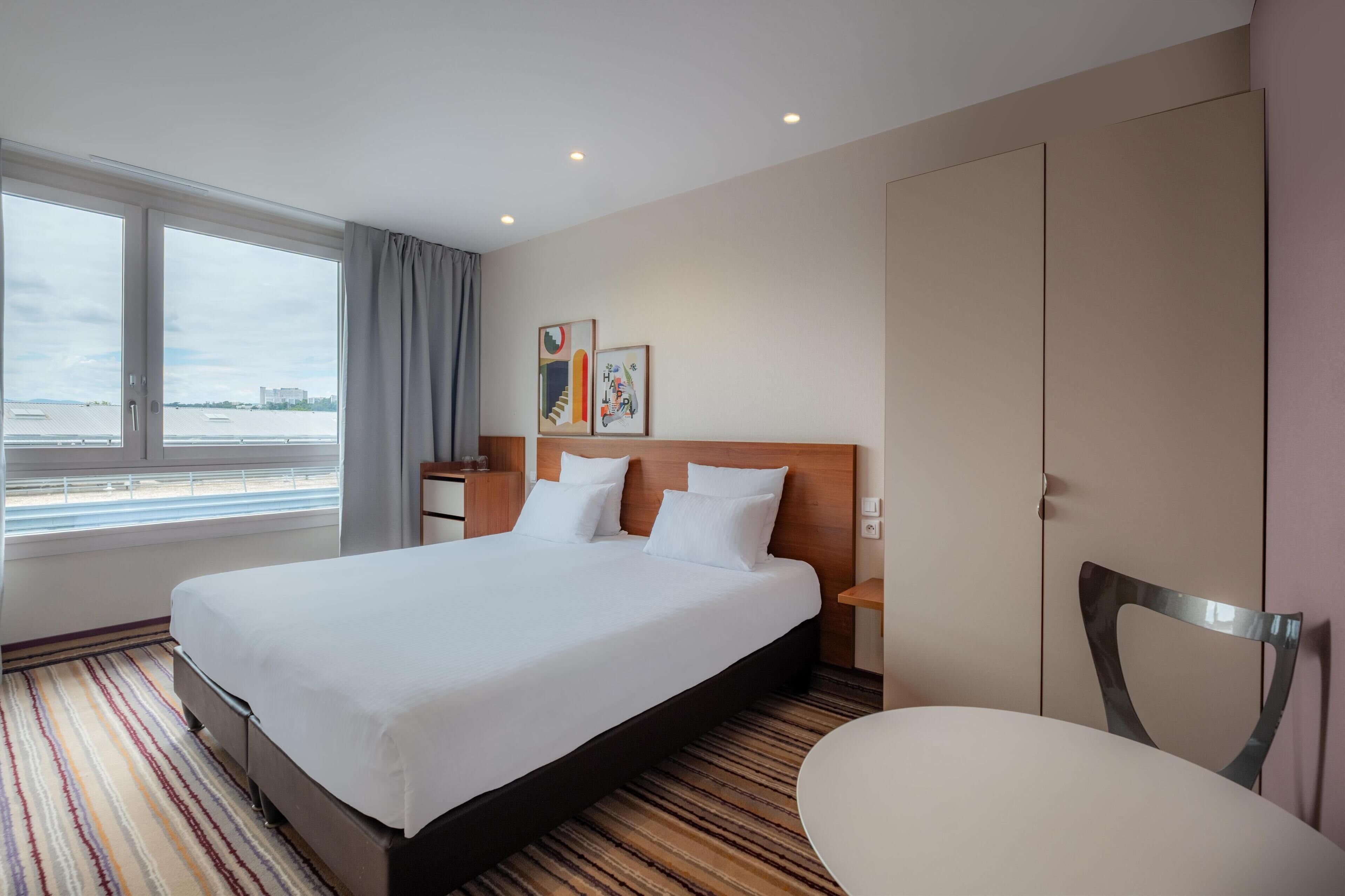 Quarto de hotel com uma cama grande, uma cadeira, uma mesa e uma janela com vista para a água.