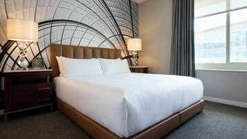 Quarto de hotel com uma cama grande, duas mesas de cabeceira, uma parede com padrão geométrico e uma janela com cortinas.