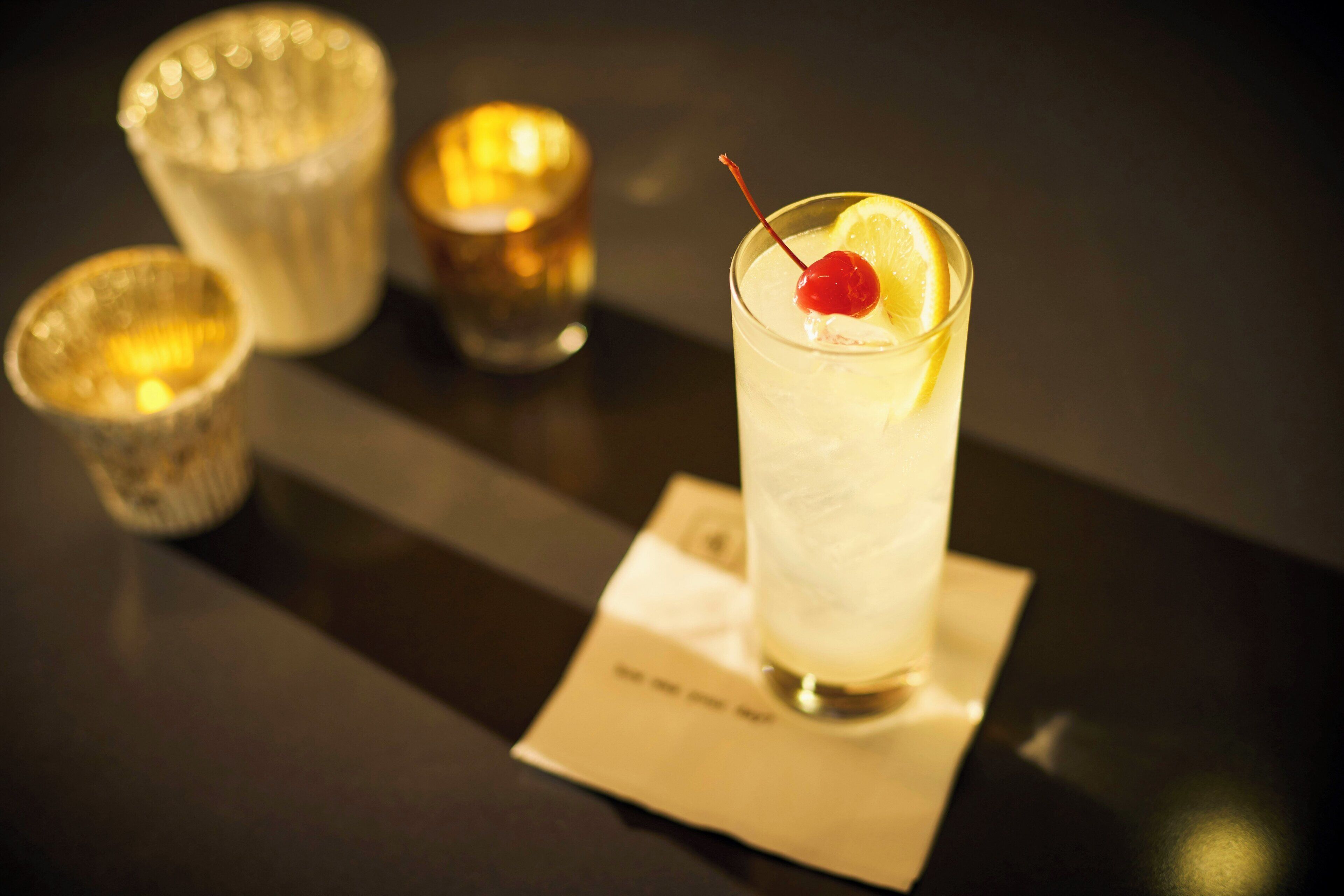 Um copo de cocktail com cereja sobre um apoio, acompanhado por dois castiçais.