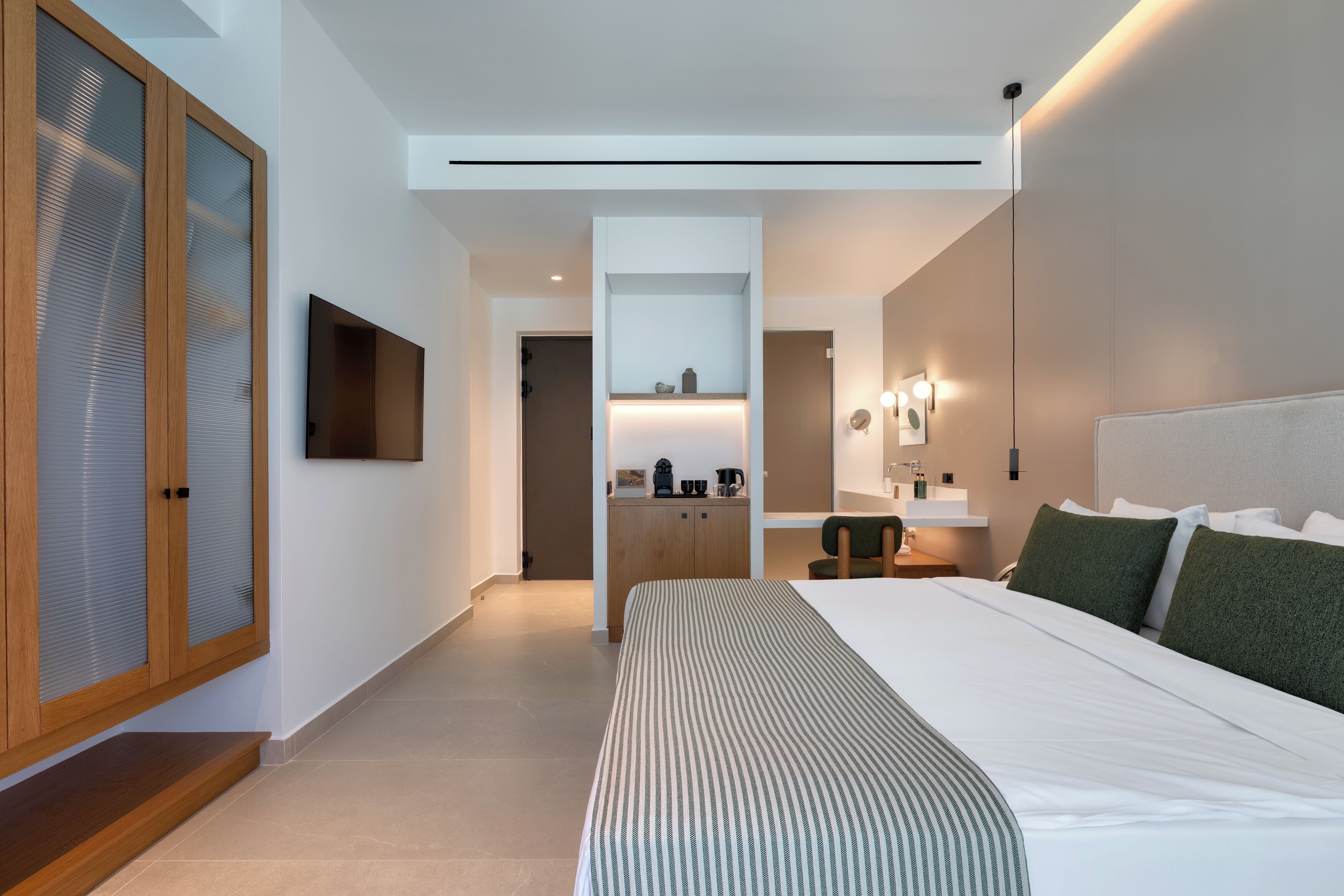 Quarto de hotel moderno com uma cama grande, televisão, cozinha compacta e banheiro.