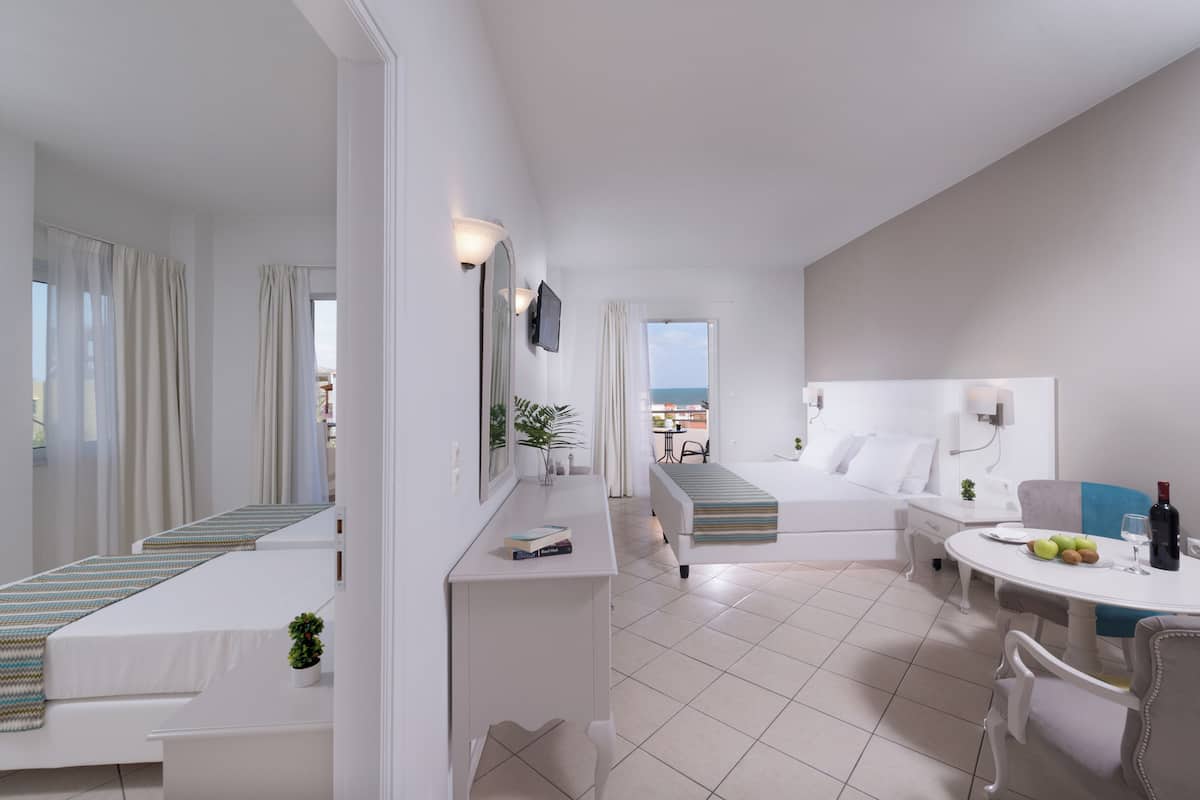 Quarto de hotel moderno com cama, escrivaninha, cadeira, mesa de jantar e vista para o mar.