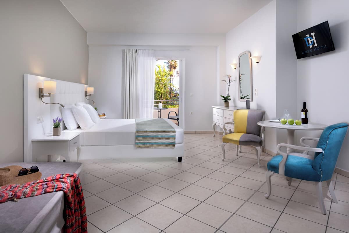 Quarto de hotel moderno com cama, escrivaninha, cadeira, mesa pequena e televisão na parede.