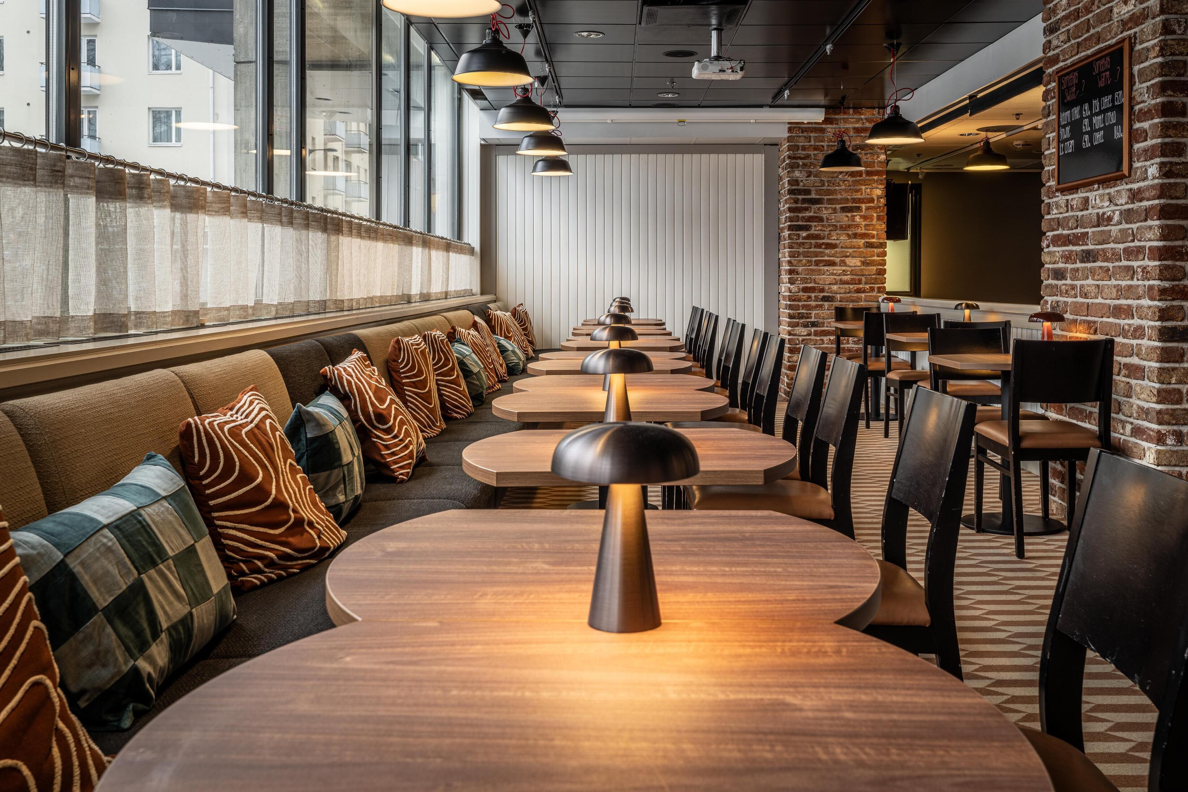 Um restaurante moderno com mesas redondas, assentos acolchoados, iluminação pendente e paredes de tijolo.