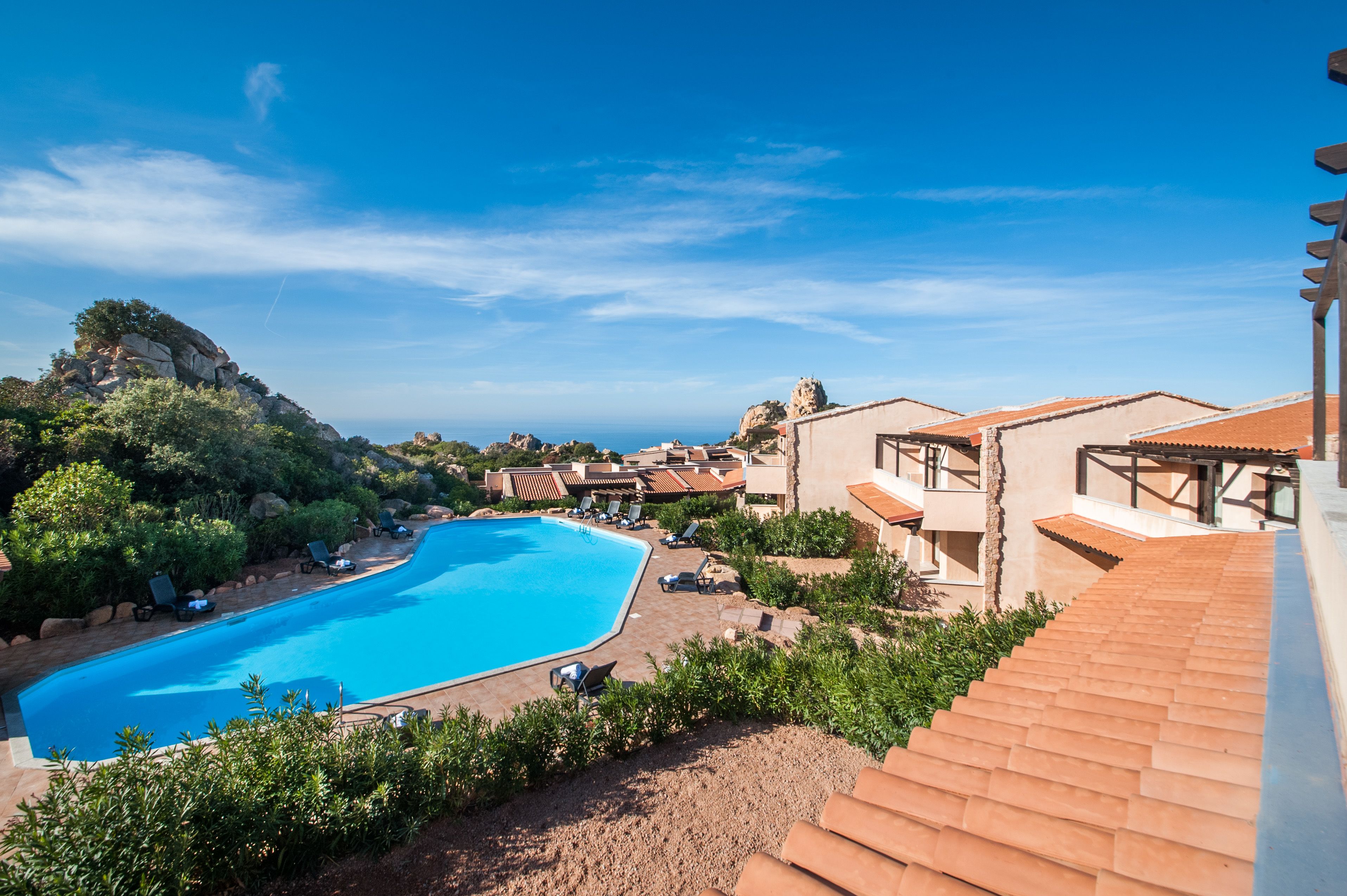 Uma piscina com espreguiçadeiras, vista para o mar e edifícios em terraços.