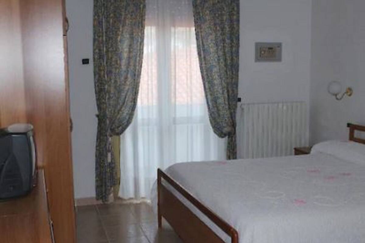 Quarto com cama, cortinas, radiador e porta de madeira.