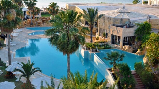 Um resort com uma grande piscina, palmeiras e vista para o mar.