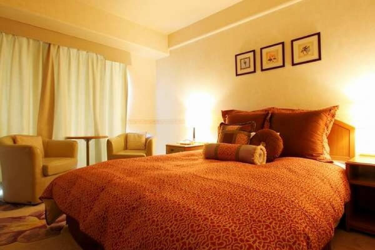 Quarto de hotel com uma cama grande, uma cadeira, uma mesa de cabeceira e uma parede com três quadros.