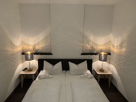 Quarto de hotel com uma cama grande, duas mesas de cabeceira com abajures e uma obra de arte na parede.