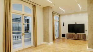 Quarto espaçoso com uma televisão grande, piso de madeira e porta de vidro que dá para uma varanda.