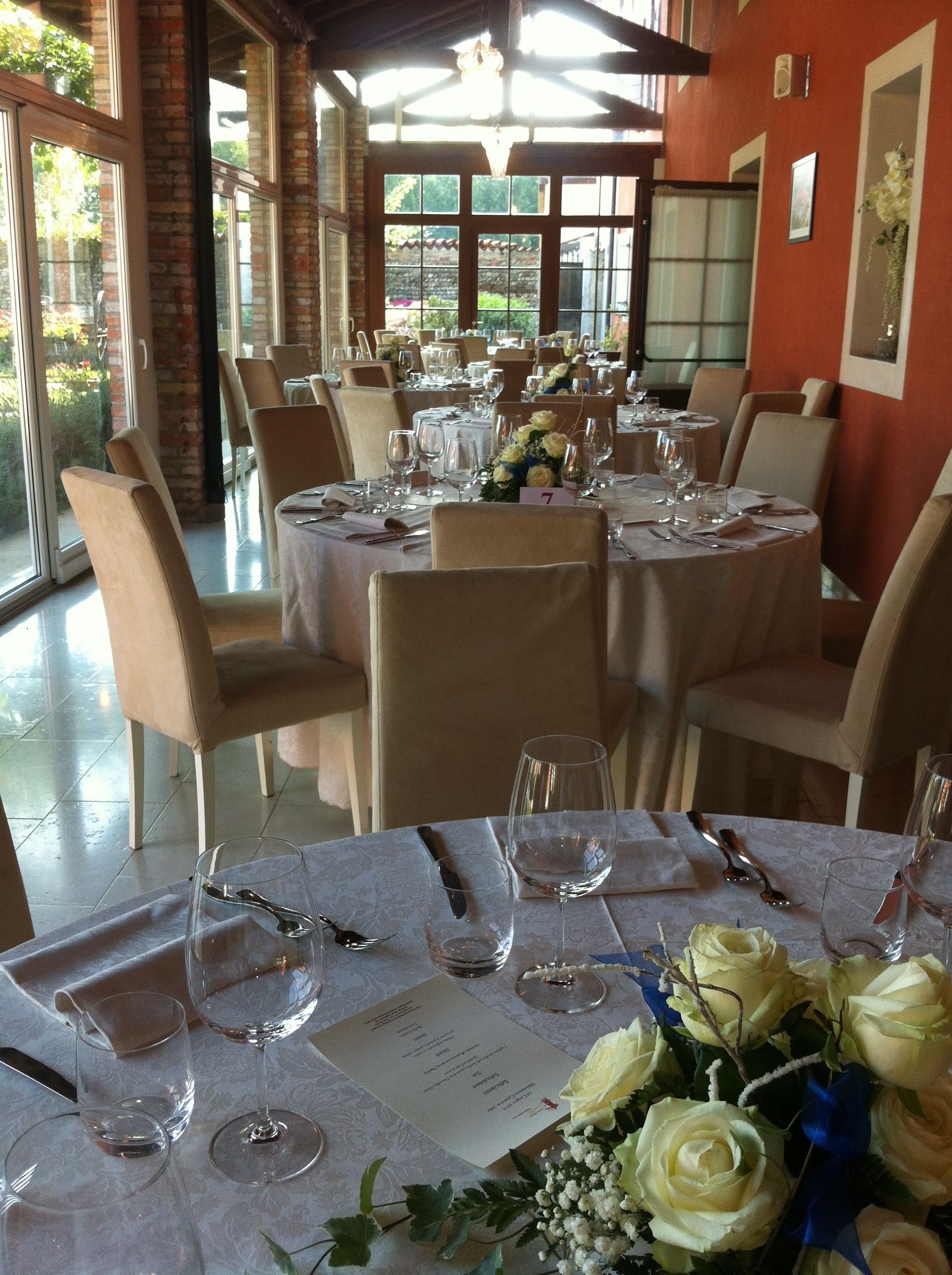 Um restaurante com mesas redondas preparadas para refeições, com toalhas brancas, cadeiras e centros de mesa florais.