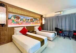 Quarto de hotel com duas camas de solteiro, um quadro na parede, uma escrivaninha com cadeiras e uma janela com cortinas.
