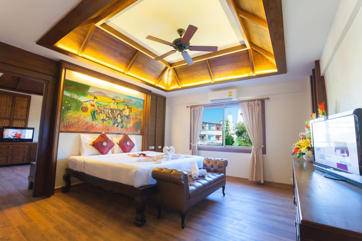 Quarto de hotel com uma cama grande, teto de madeira, televisão e janela com cortinas.