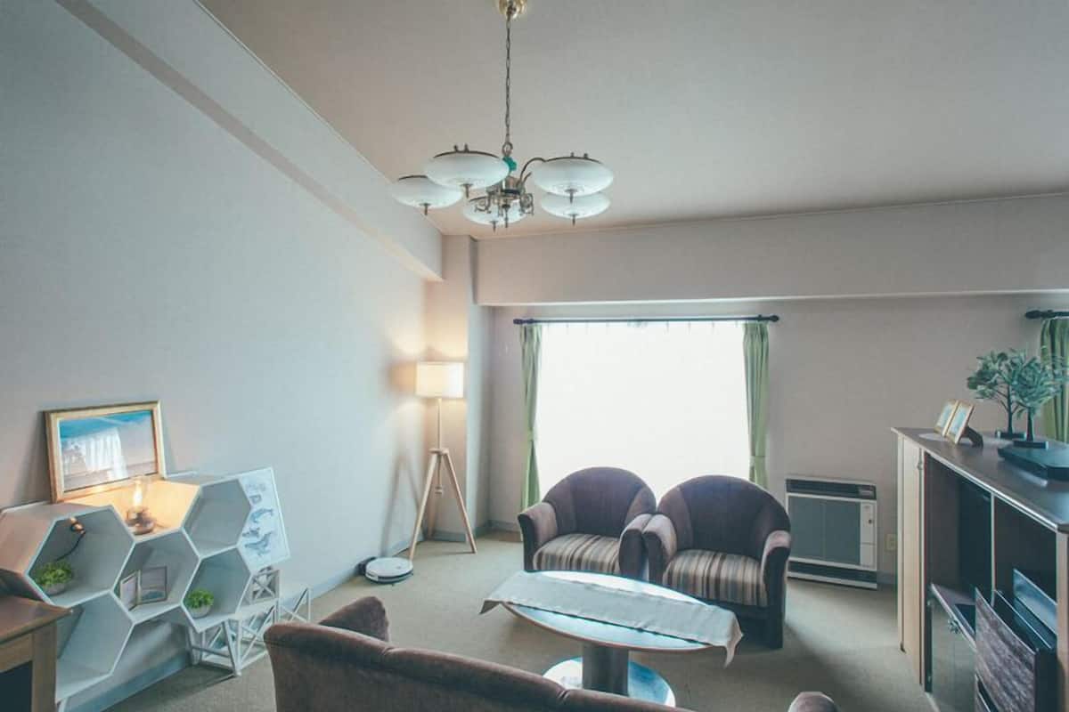 Uma sala de estar com sofá, mesa de centro, luminária, módulo de armazenamento hexagonal e uma grande janela com cortinas.