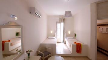 Quarto de hotel com duas camas de solteiro, área de estar com uma poltrona e mesa, espelho e luminária suspensa.