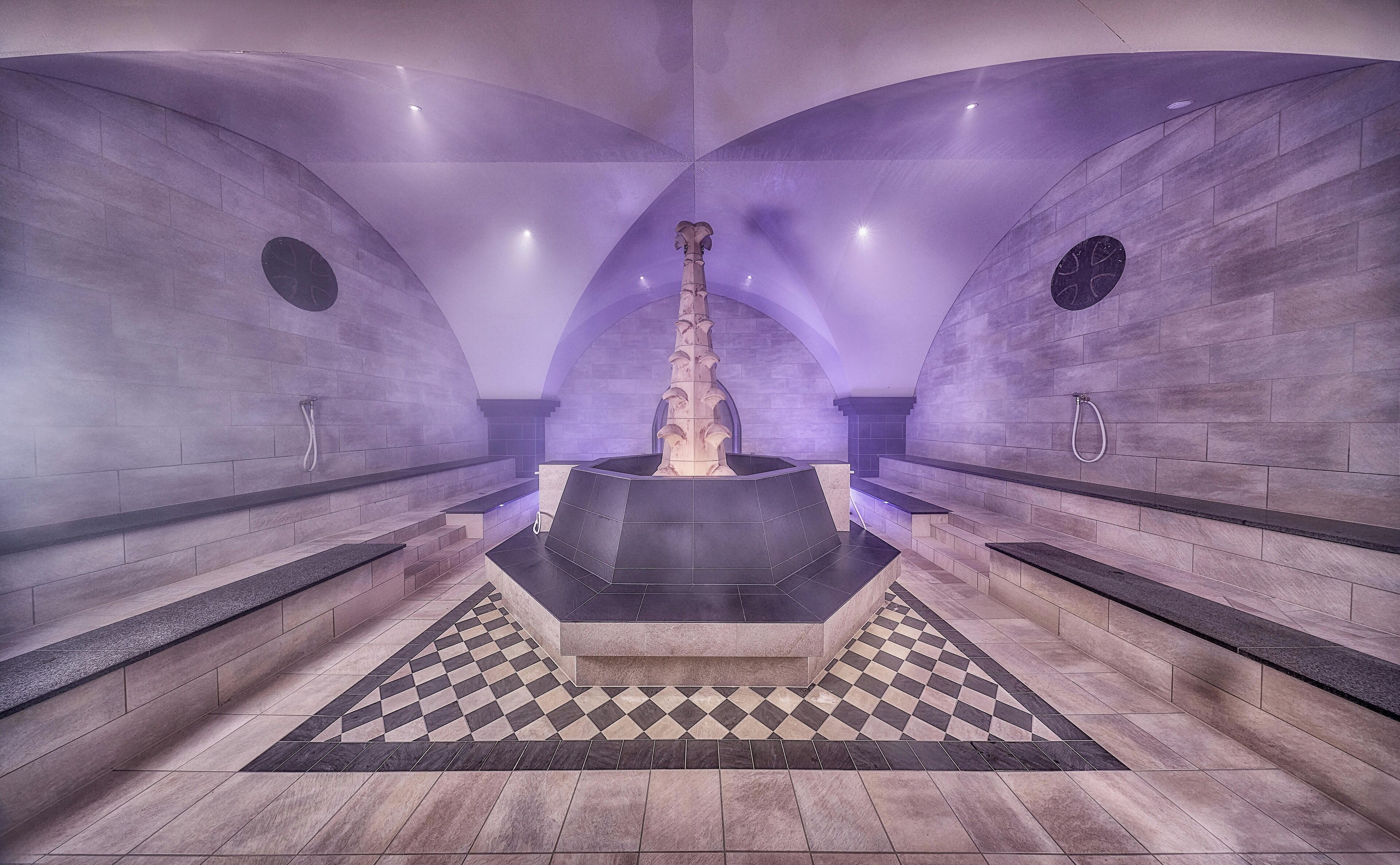 Uma sauna com um pilar central, chão xadrez e teto em arco.