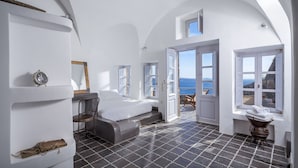 Um quarto espaçoso com uma cama, uma poltrona, uma mesinha e vista para o mar.