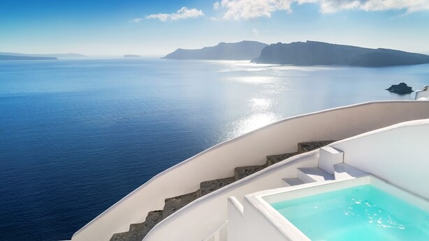 Vista de uma piscina com escadaria que leva a uma varanda com vista para um corpo d'água e formações terrestres ao longe.