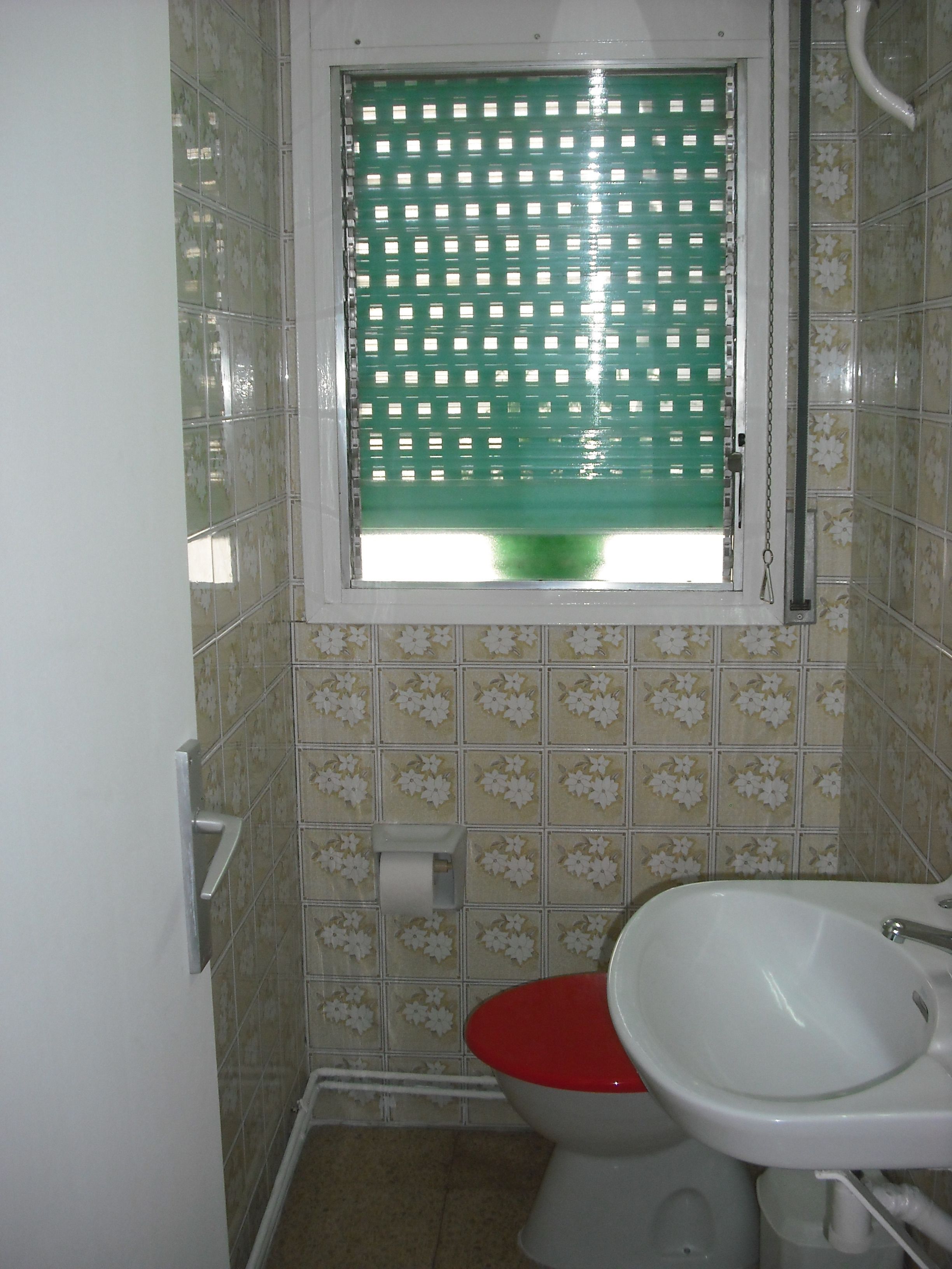 Um banheiro pequeno com vaso sanitário, pia e janela com tela verde.