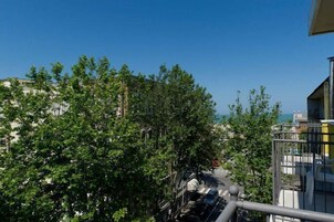 Uma varanda com vista para uma rua arborizada e um prédio do outro lado da rua.