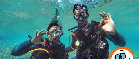 Dois mergulhadores de cilindro debaixo d'água, com o logotipo de 'SKOPELOS DIVE CENTER' no canto inferior direito.