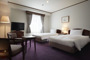 Quarto de hotel com duas camas, televisão, escrivaninha e uma cadeira.