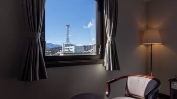 Quarto de hotel com vista para uma torre e montanhas através de uma janela, uma cadeira e um abajur.