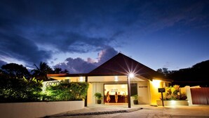 Um resort chamado 'Geckos', com uma área de recepção, uma placa indicando 'Acesso Exclusivo para Desembarque' e arredores bem iluminados.