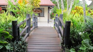 Uma ponte de madeira leva a uma loja de artigos de luxo e artesanato, cercada por vegetação exuberante.