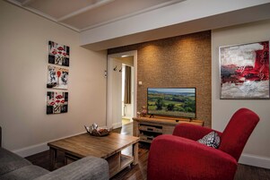 Uma sala de estar com uma mesa de centro de madeira, uma poltrona vermelha e uma televisão de tela plana em um suporte de madeira.