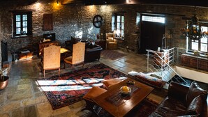 Um interior rústico com paredes de pedra, lareira, mobiliário de couro e um candelabro.