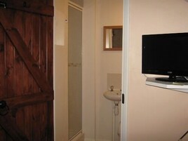 Um banheiro com porta de madeira, pia branca e televisão fixada na parede.