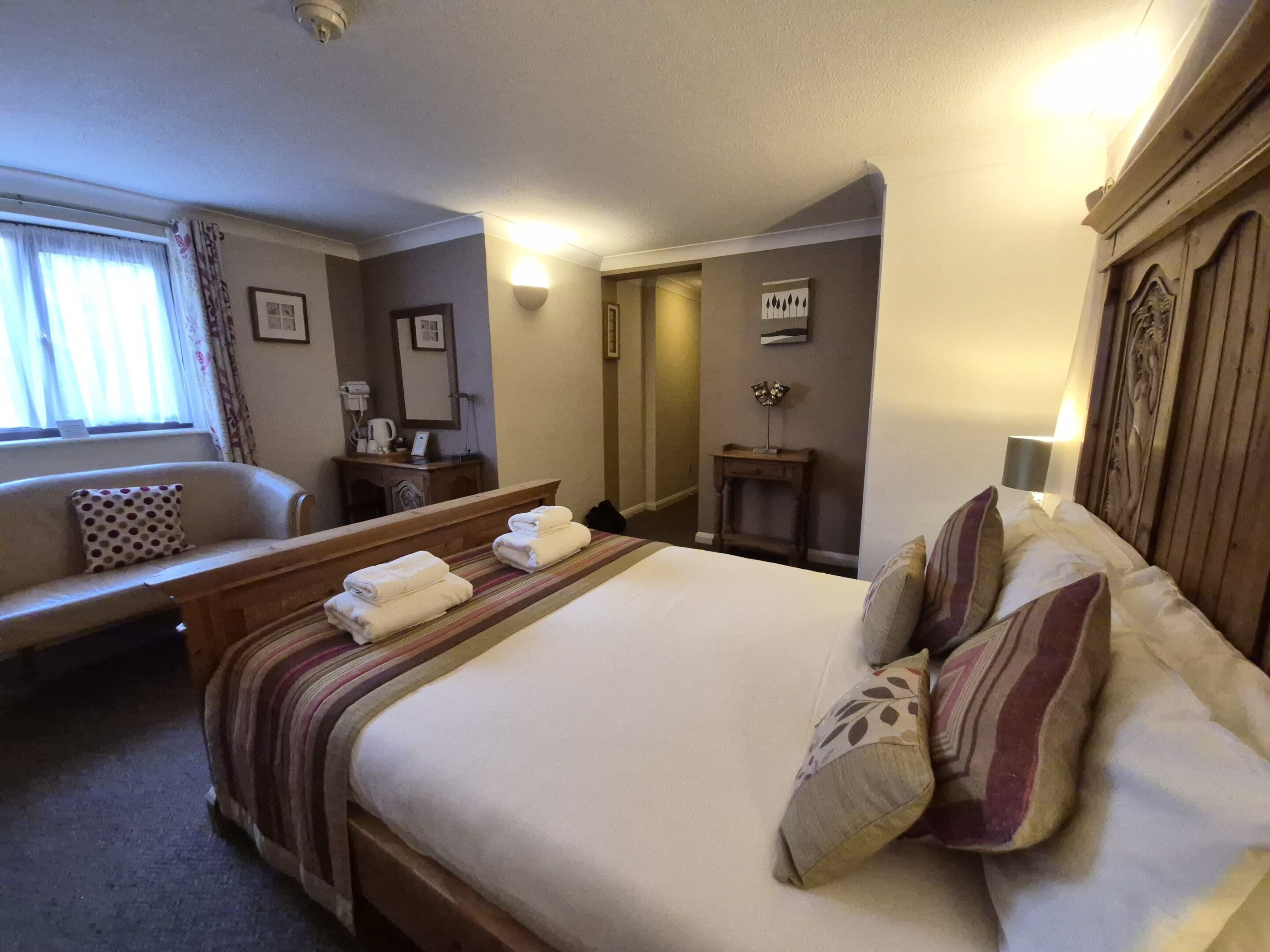 Quarto de hotel com cama, sofá, escrivaninha e espelho.