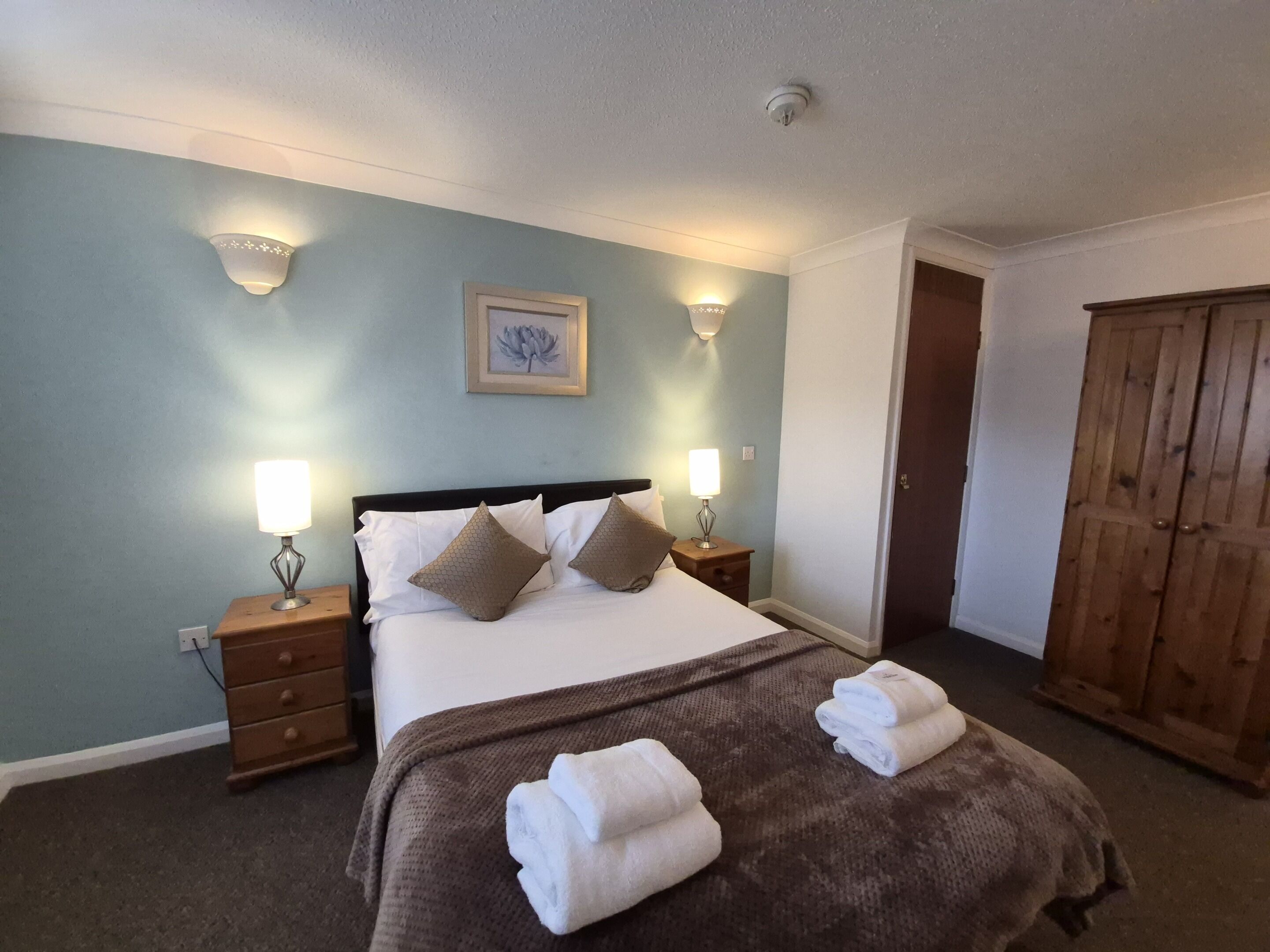 Quarto com cama, duas mesas de cabeceira com luminárias, um armário de madeira e um quadro na parede.