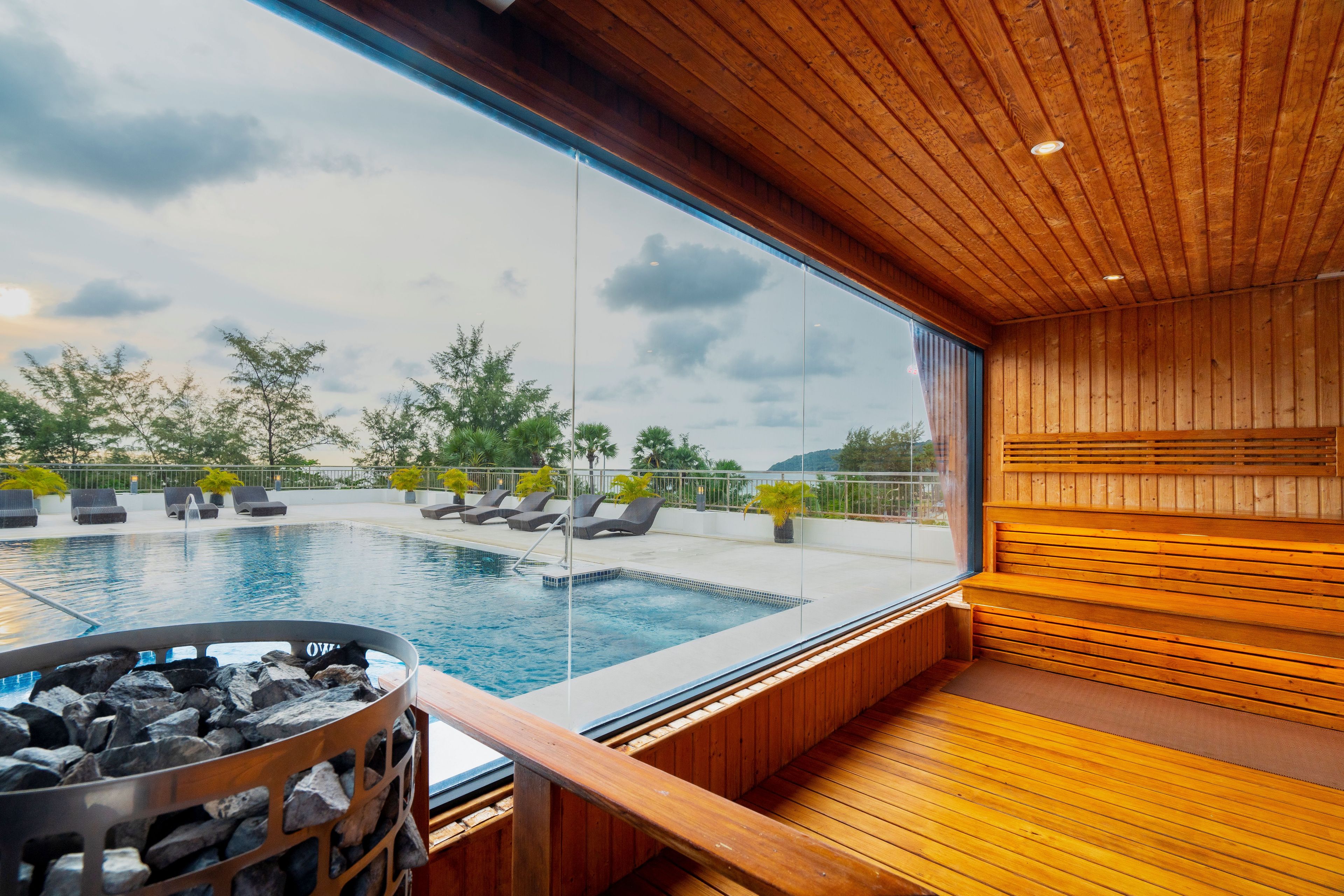 Uma área interna de piscina moderna com vista para o céu e árvores, piso de madeira e cadeiras de descanso.