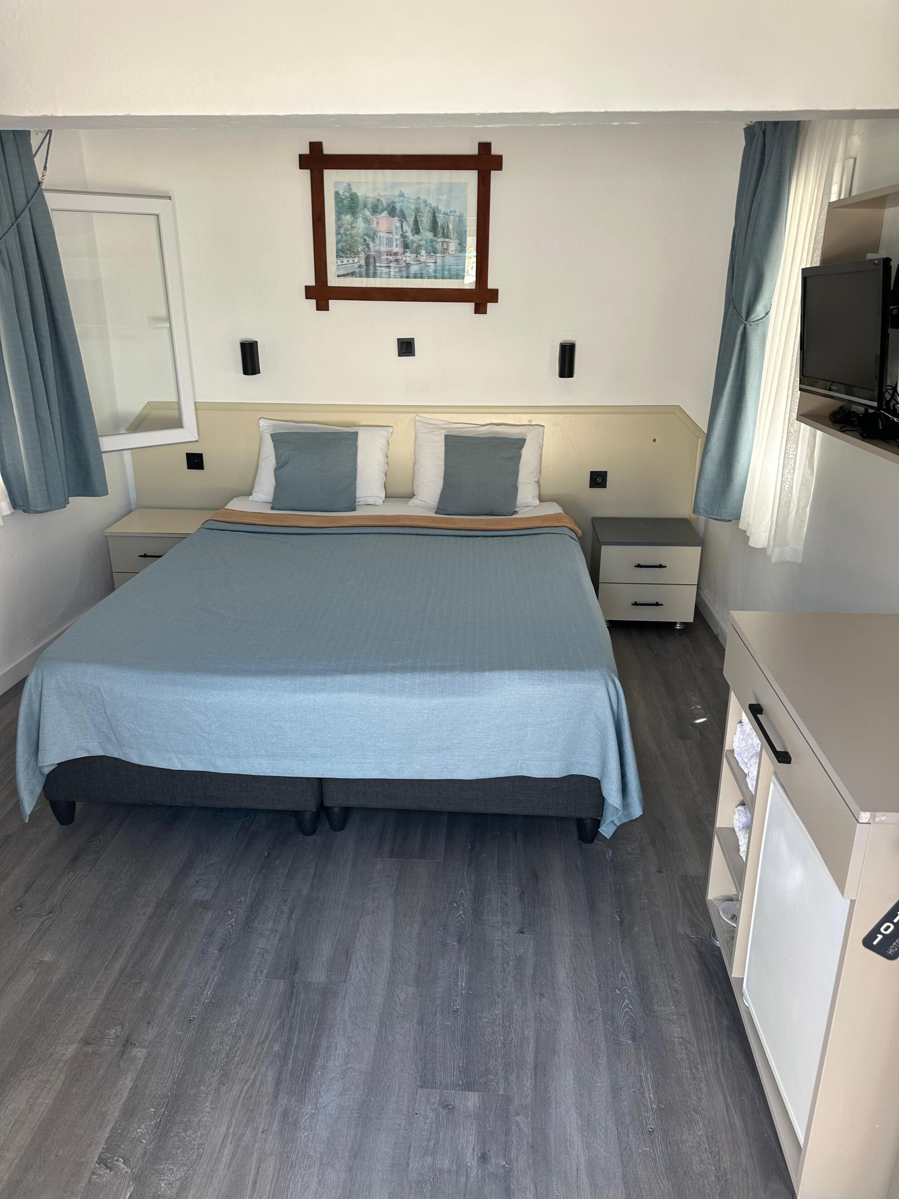 Quarto com cama, mesas de cabeceira, televisão e um quadro na parede.