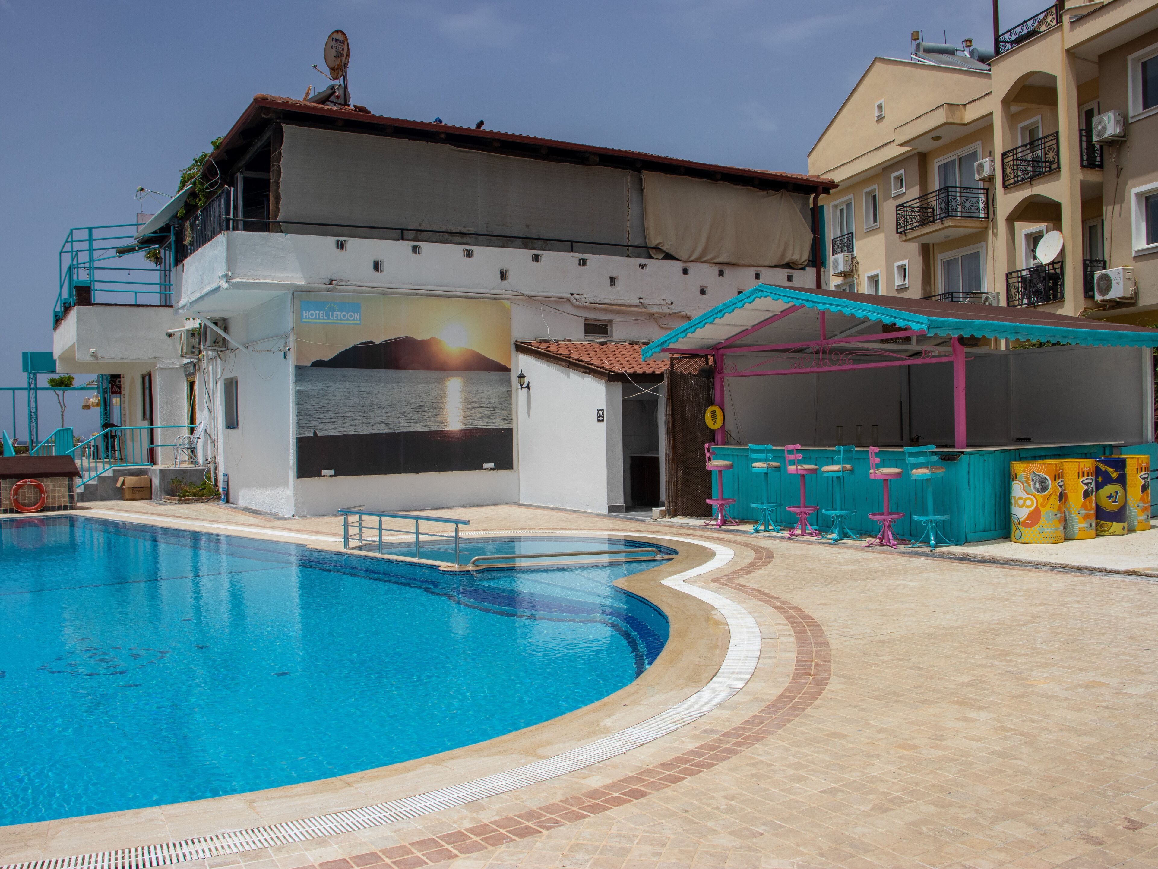 Hotel com piscina, área de bar coberta e um mural de um pôr do sol sobre a água.