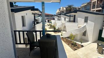 Uma área externa coberta com mesa e cadeiras, vista para casas vizinhas e um céu azul claro.