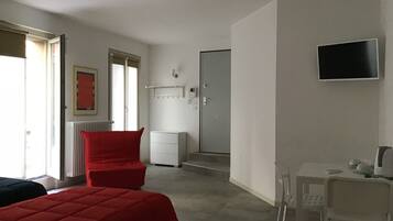 Quarto de hotel com cama, mesa, cadeira, televisão e porta do banheiro.