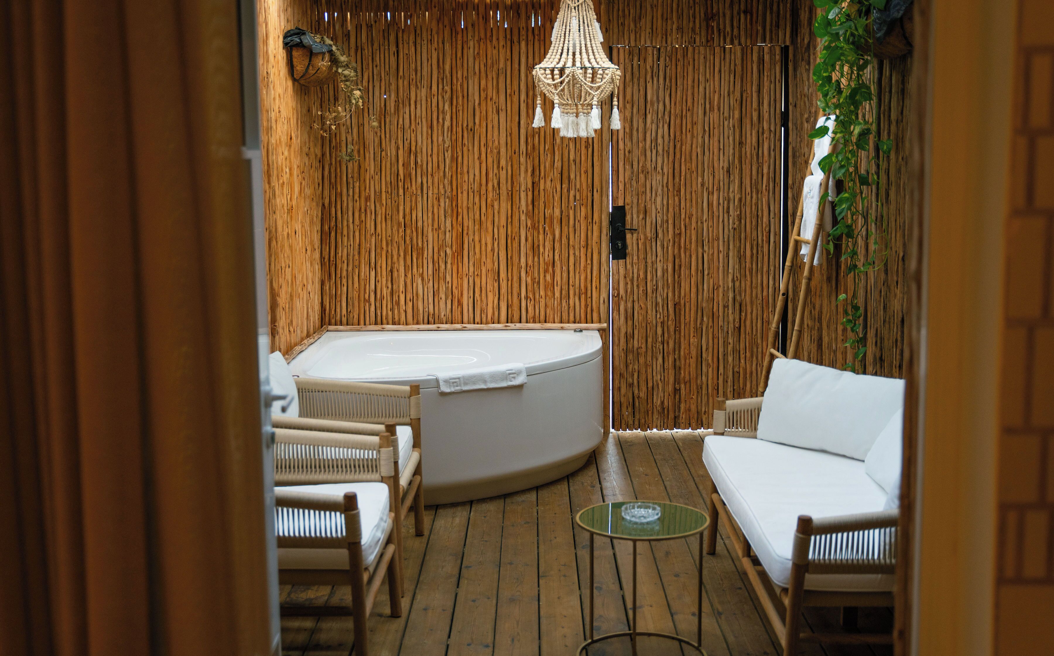 Um quarto de spa com parede de madeira, uma banheira de hidromassagem, dois sofás brancos e uma pequena mesa.