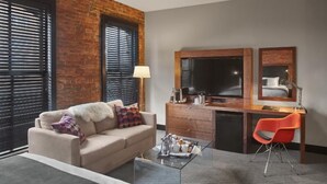 Quarto de hotel moderno com parede de tijolos, um sofá, uma escrivaninha com computador e televisão.